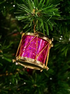 A small decorative drum ornament hanging on a Christmas tree, shining in pink and gold colors. The close-up view shows fine details and festive charm, photographed indoors in Kozhikode, Kerala.  